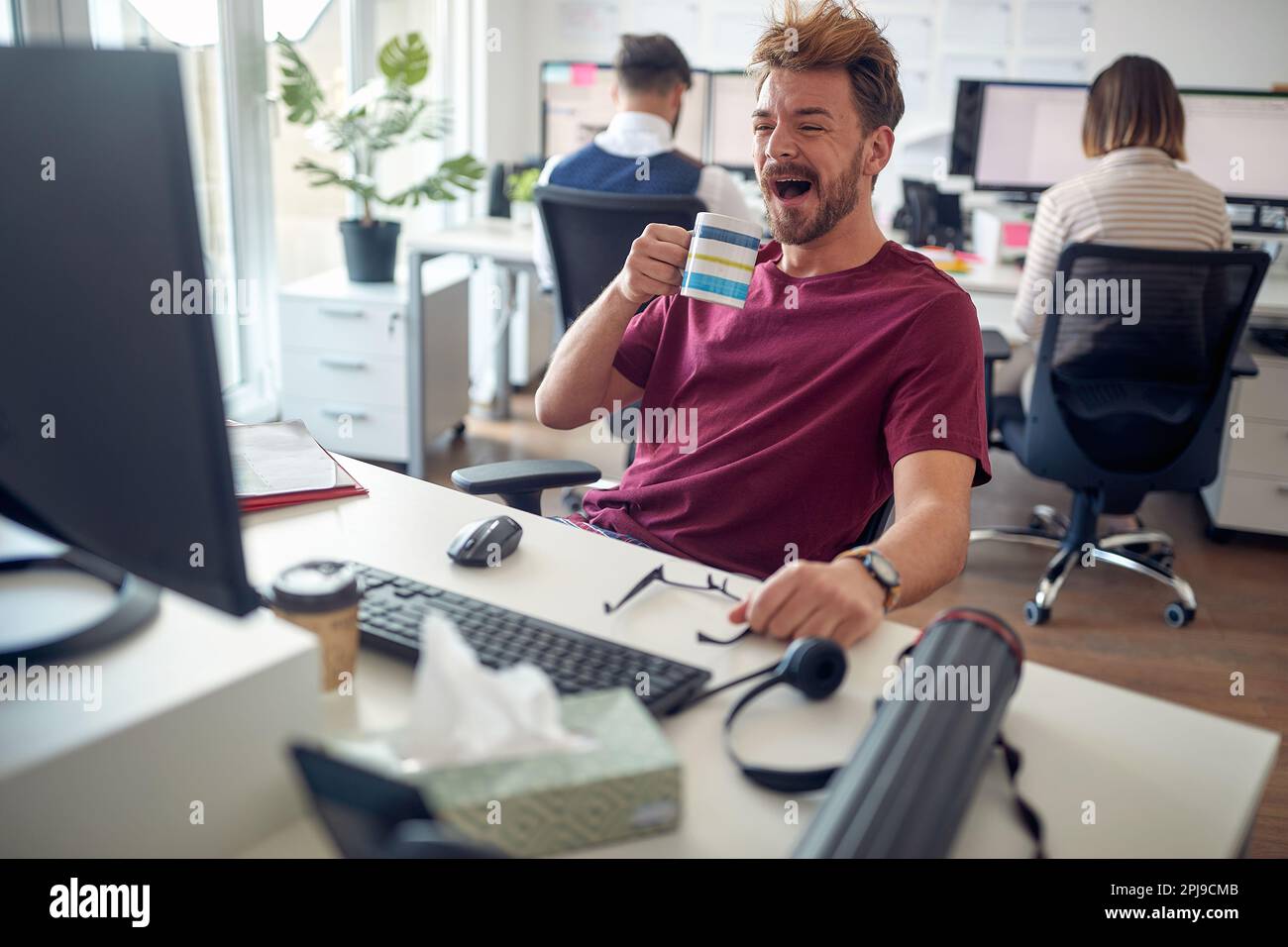 A tired male employee in a pleasant atmosphere in the office is trying ...