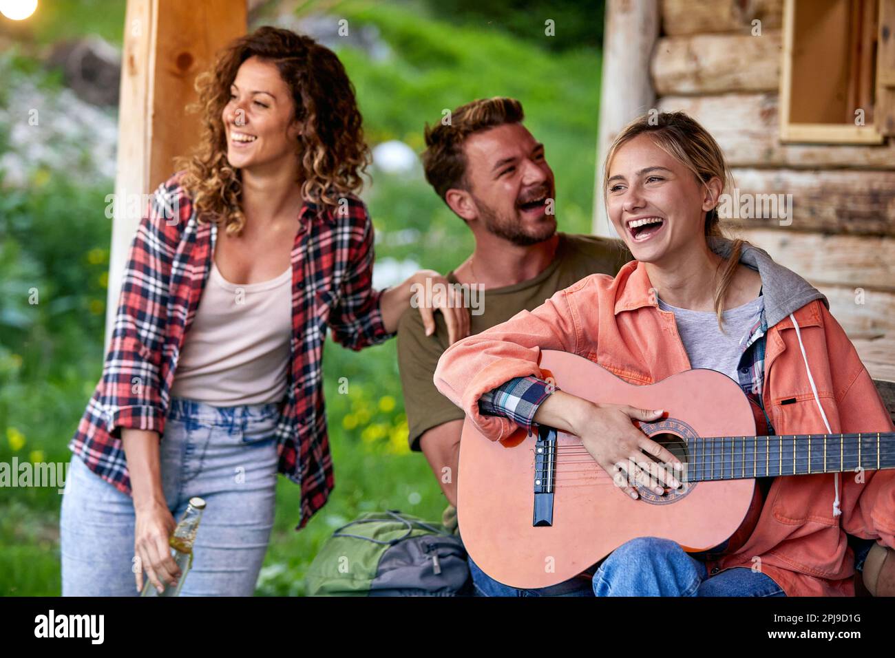 Three cheerful young friends enjoying vacation day and playing guitar ...
