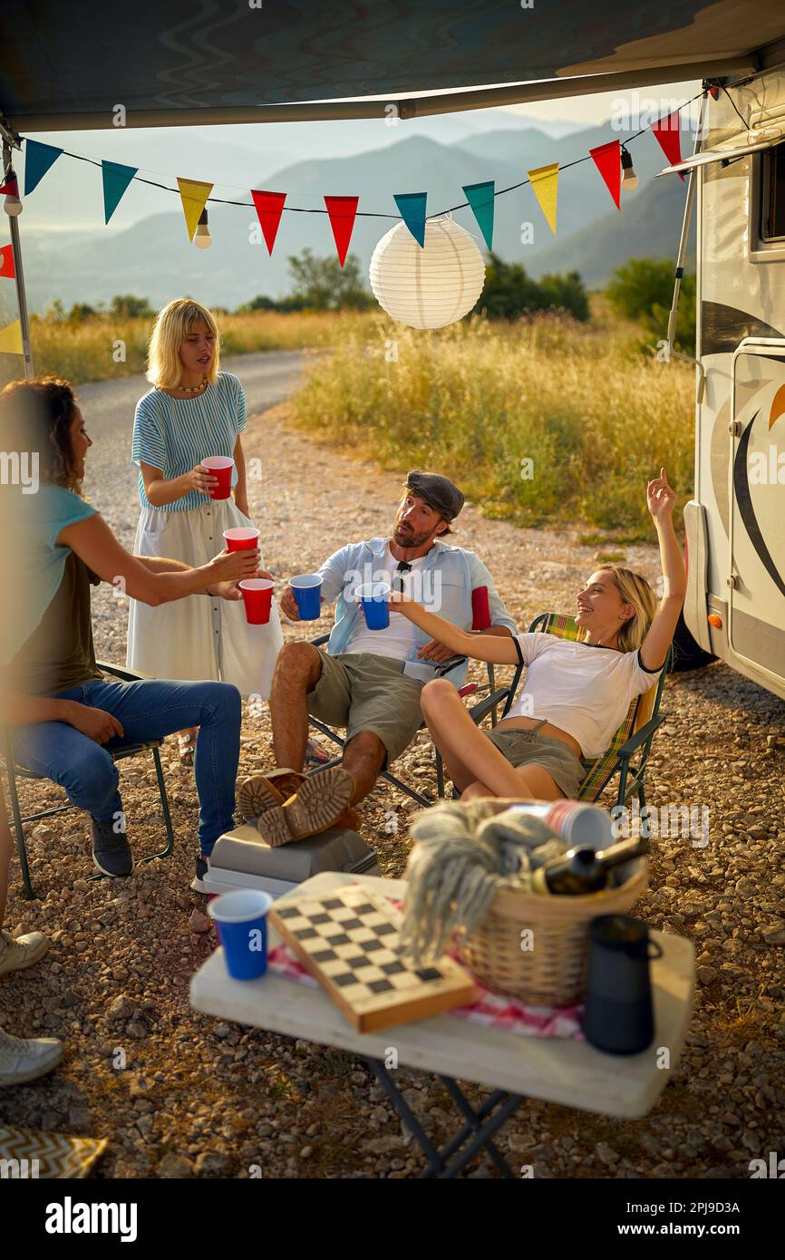 Group of friends in front of camper rv sitting and cheering with drinks ...