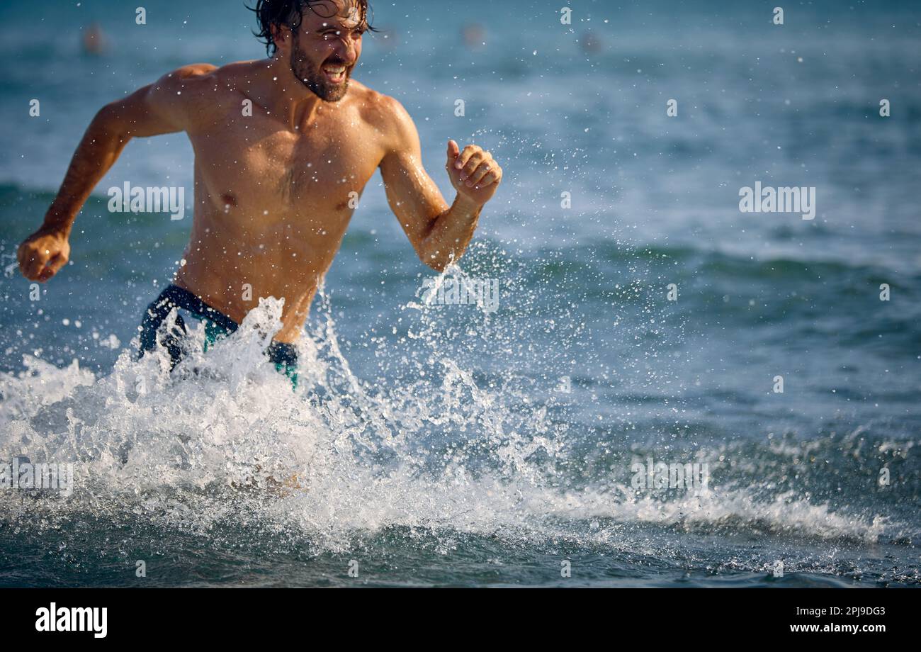 Fit handsome young man running in water at beach. Young man on vacation ...
