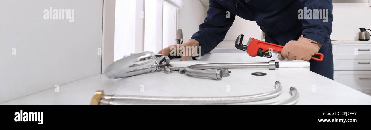 Professional plumber fixing water tap in kitchen, closeup. Banner ...