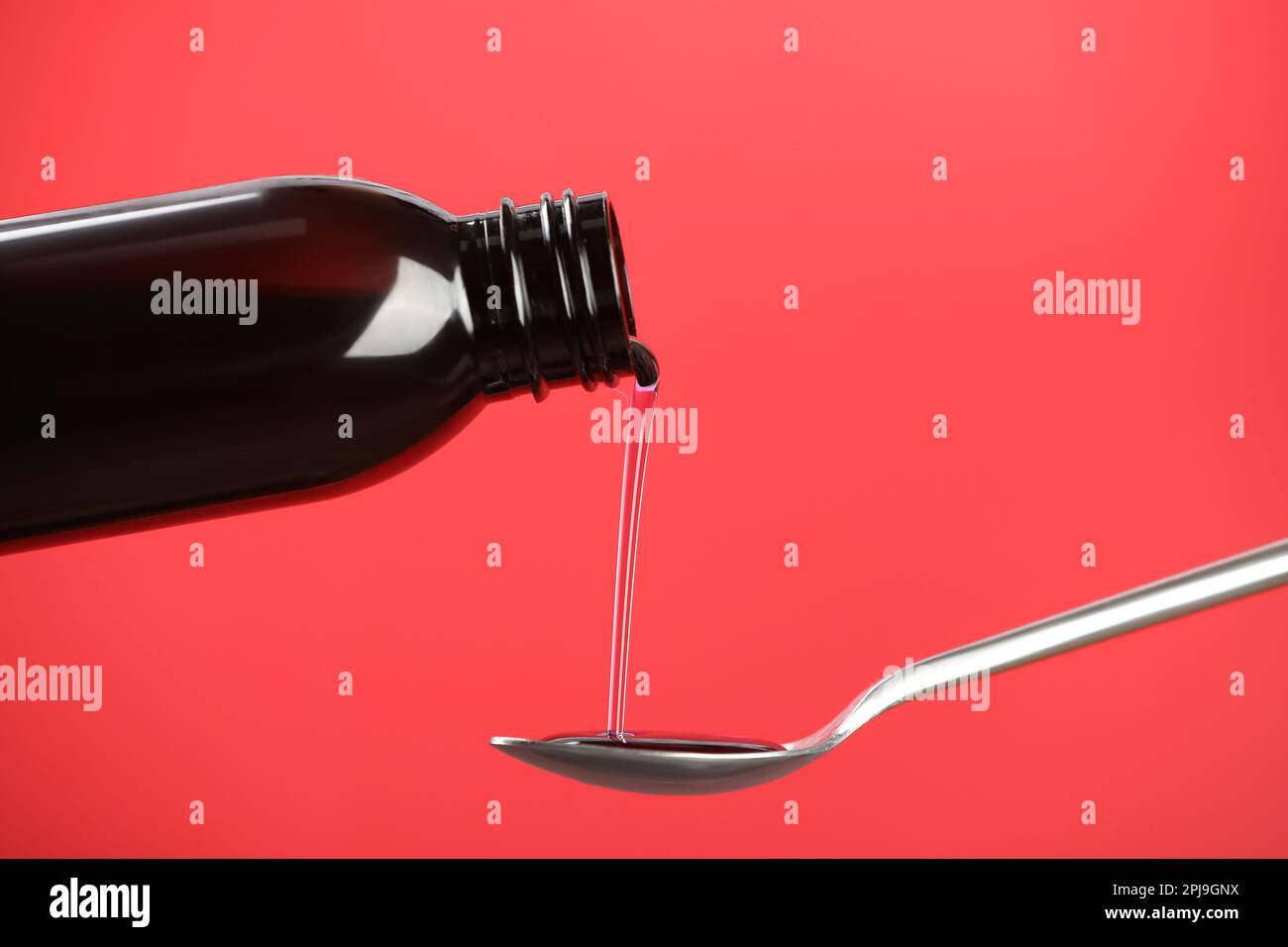 Pouring cough syrup into spoon on red background Stock Photo - Alamy