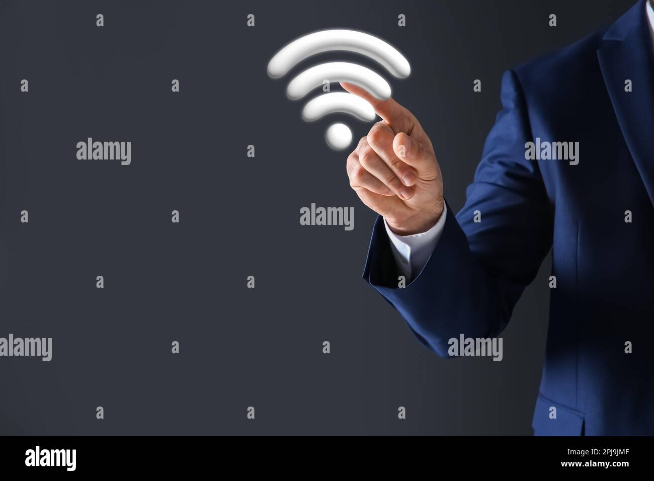 Man touching Wi Fi symbol on digital screen against dark grey ...