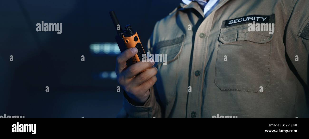 Professional security guard with portable radio set in dark room ...