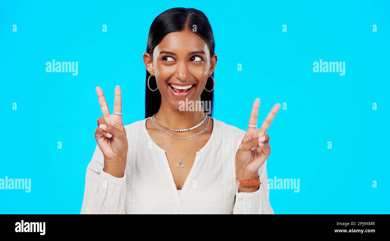 Happy woman, peace and face wink in studio, blue background and color ...