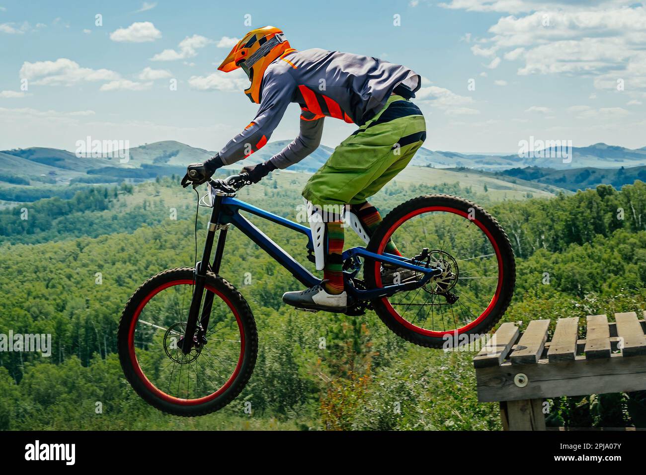 male rider on downhill bike jumping wooden drop, racing DH mountain ...