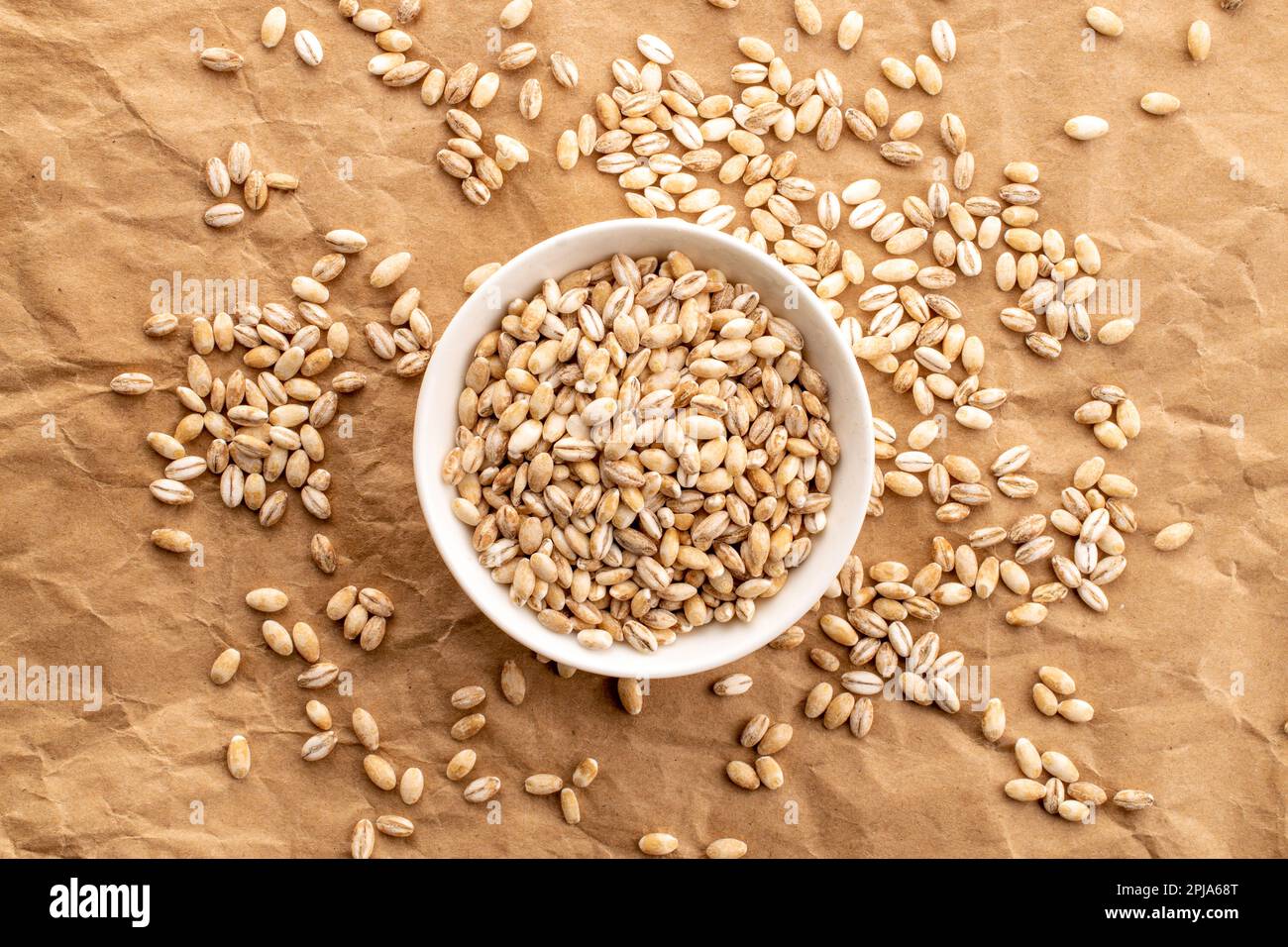Organic pearl barley in white saucer on kraft paper, close-up, top view ...