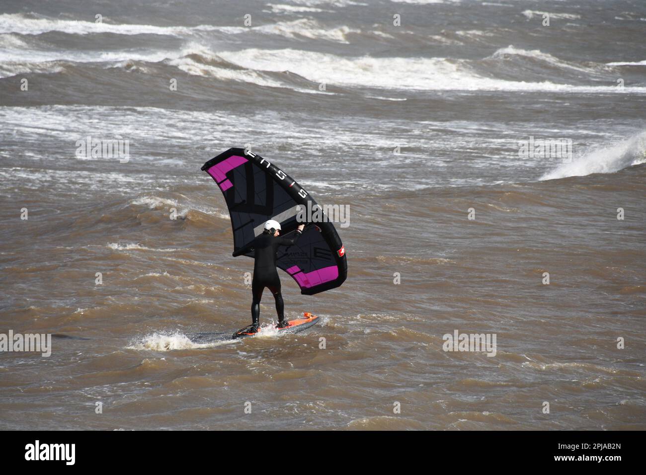 A Wing foil surfer struggles to get up onto his foil in a choppy sea ...
