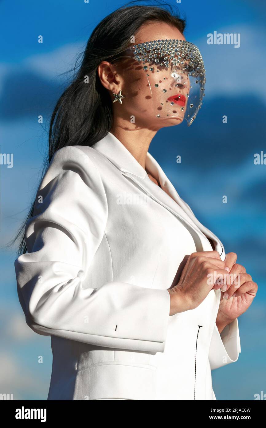 A brunette girl in a white suit with a transparent mask on her face ...