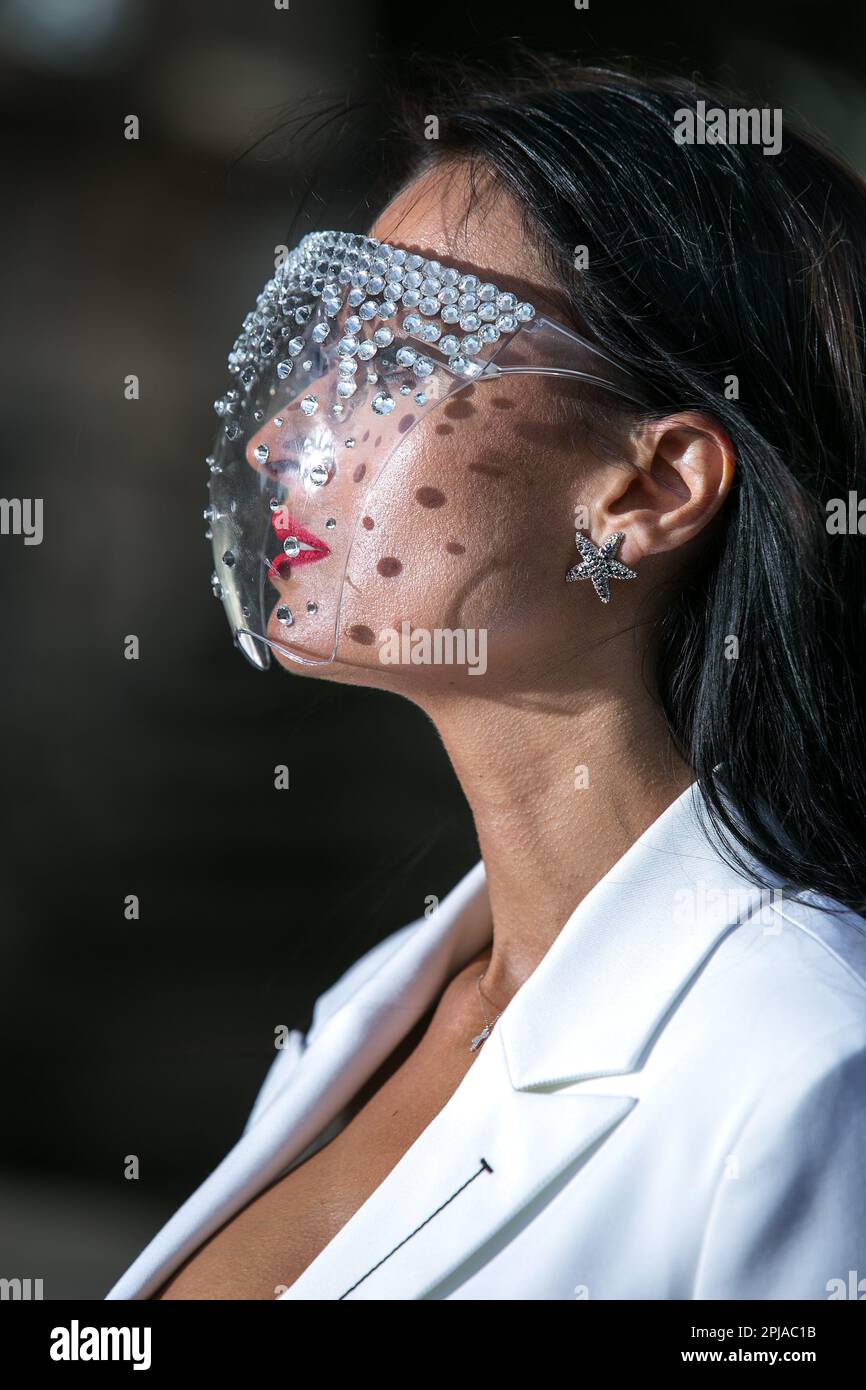 A brunette girl in a white suit with a transparent mask on her face ...