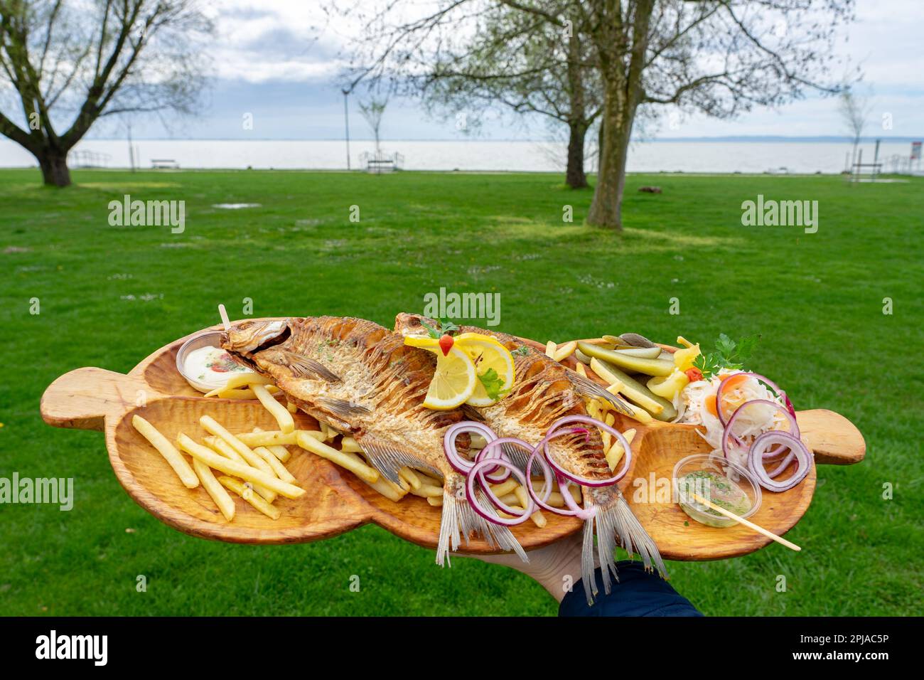 holding fried traditional bream fish platter next to lake Balaton in ...