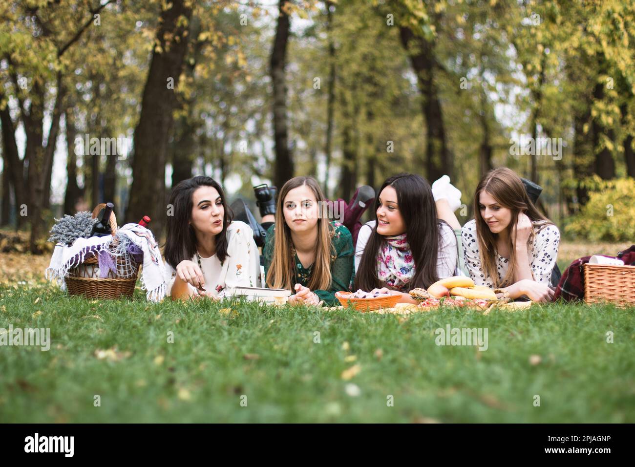Group of four women on a fun fall picnic in the park, laying on a ...