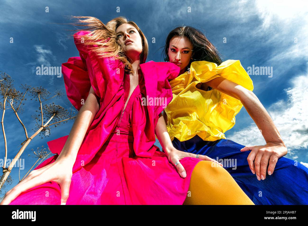 Two models in bright outfits pose against the background of nature ...