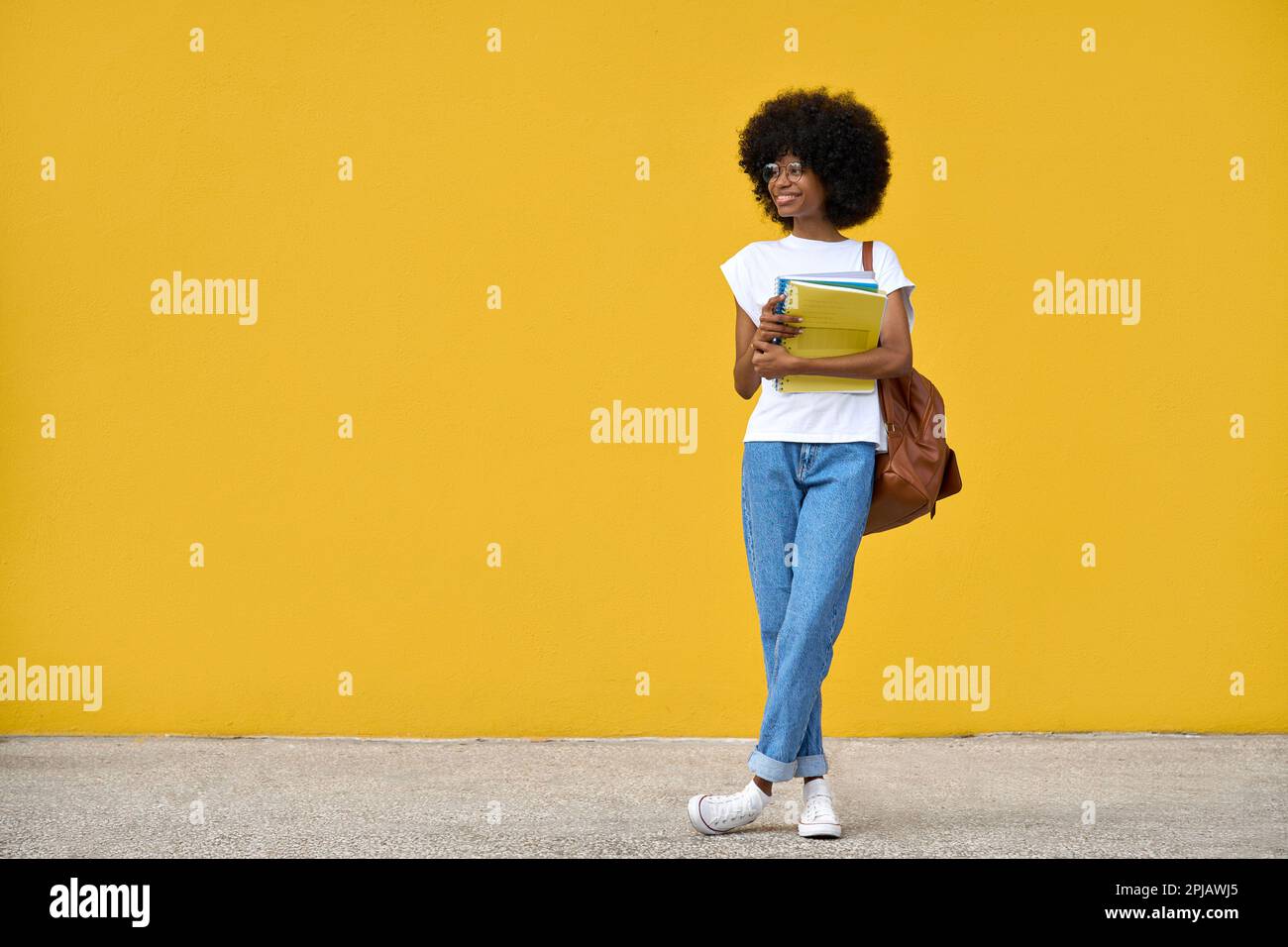 Fullbody portrait of a smart student looking aside on yellow background ...
