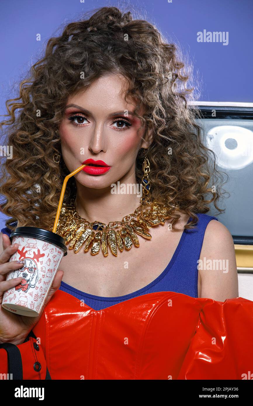 A girl in a bright outfit in the style of the 80s poses in the studio ...