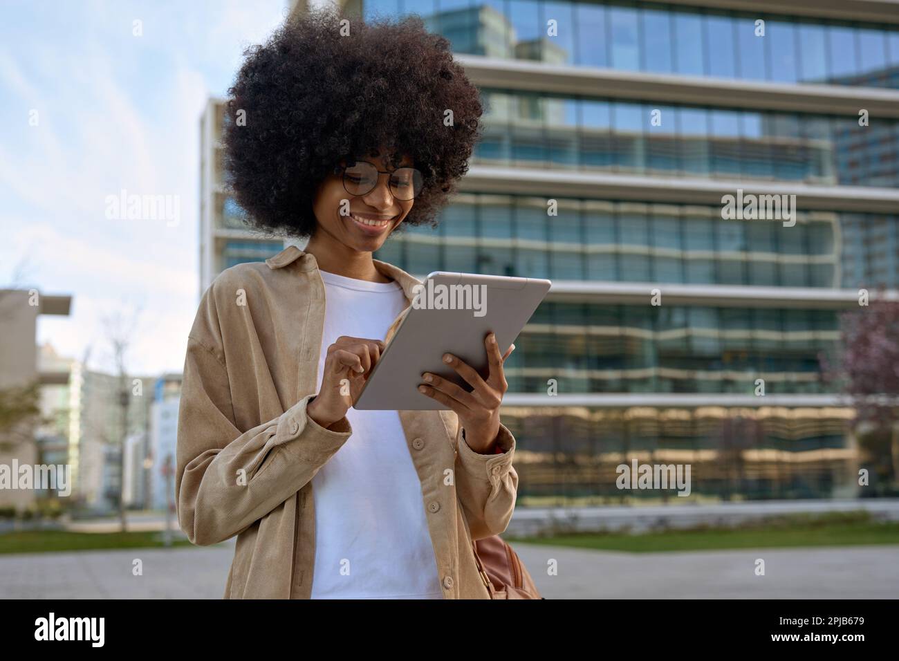 A young woman using touchscreen of tablet standing in front of ...