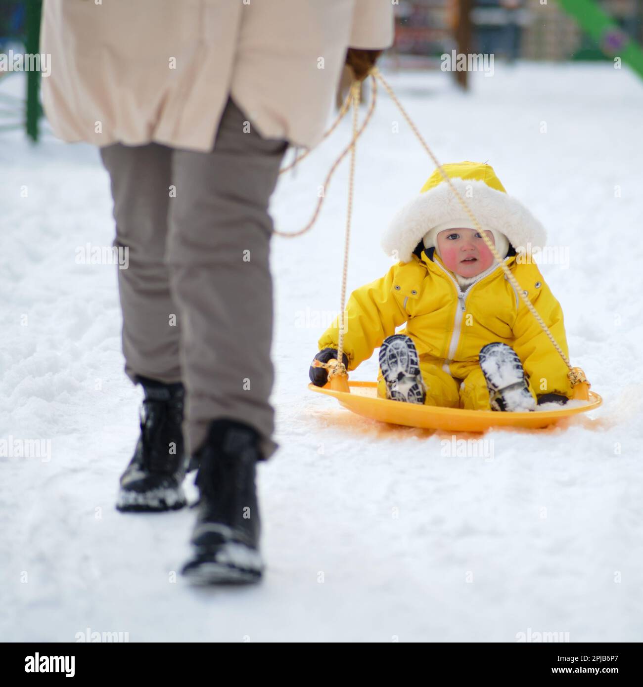 Toddler baby rides in the snow on icesled, a winter playground. Mother ...