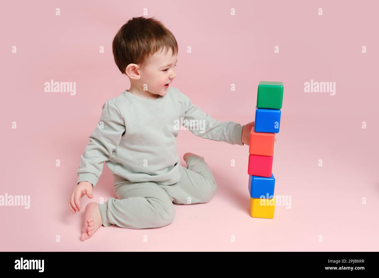 Happy toddler baby plays with cubes on studio pink background. Child ...