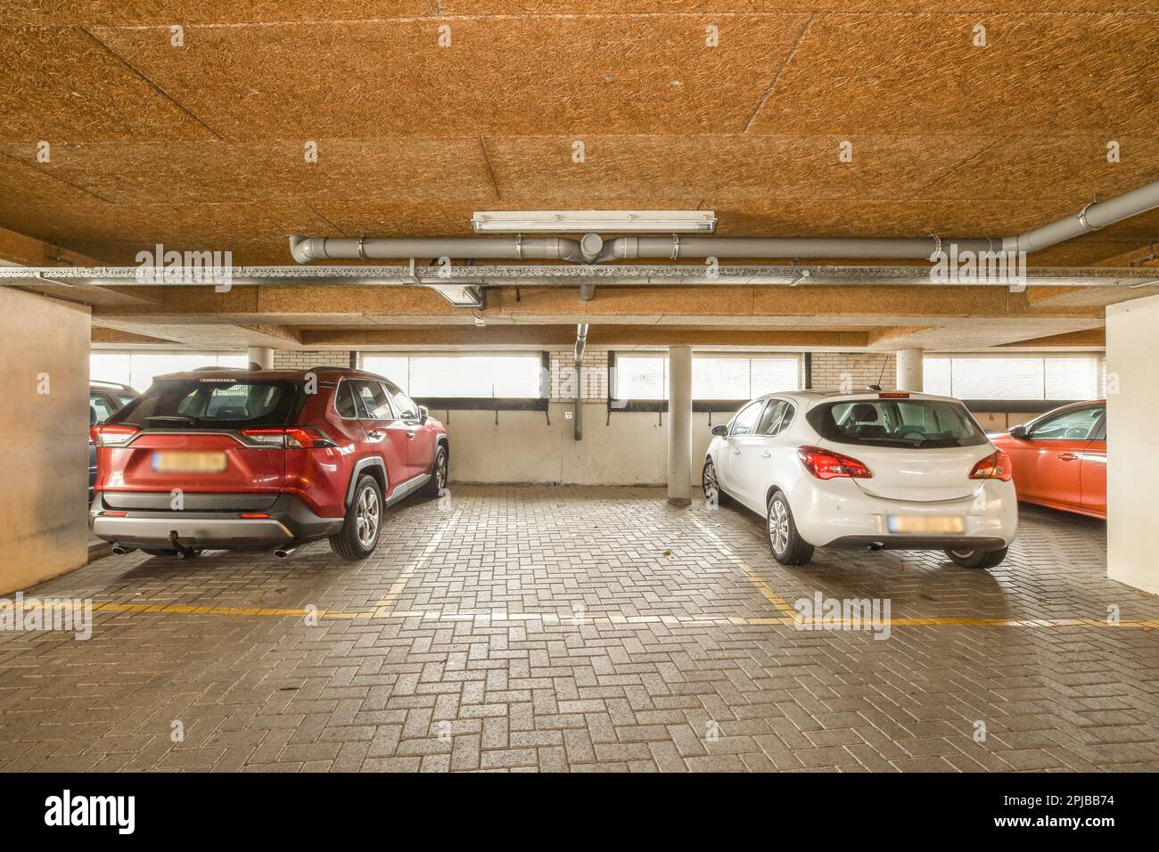 two cars parked in an underground parking space, one is red and the ...