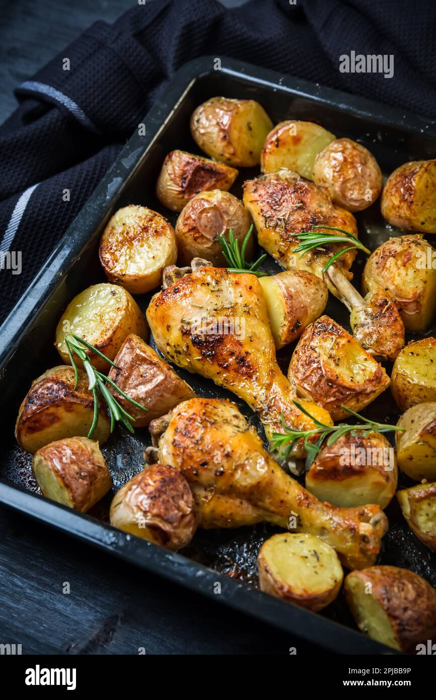 Baked hot chicken legs with spicy potatoes in baking tray on black ...