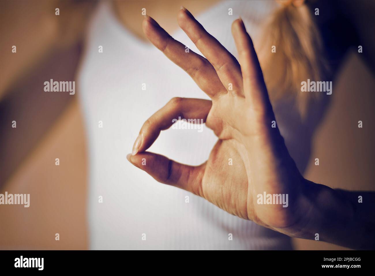 Female hand shows ok sign. Background of the young body in a white T ...