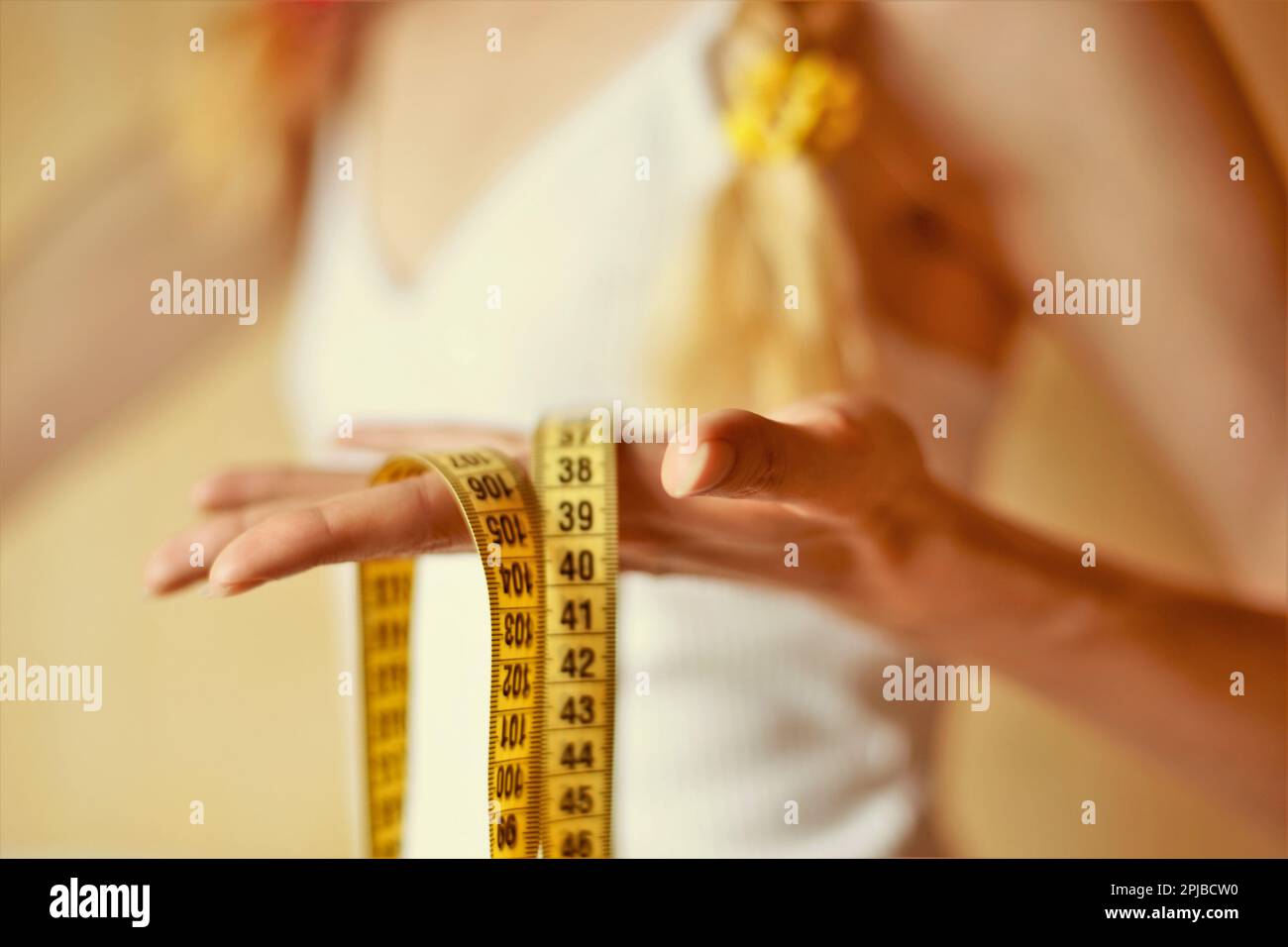 Yellow measuring tape in young female hand, closeup, side view, blurred ...