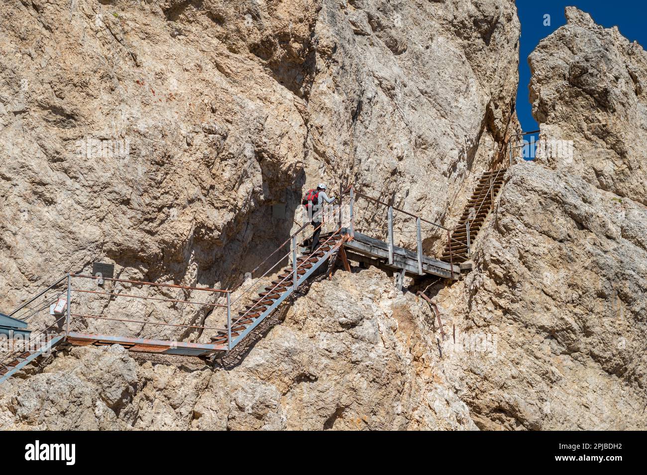 Tourist climbing steel stairs fixed to the rock. Dolomites, Italy ...