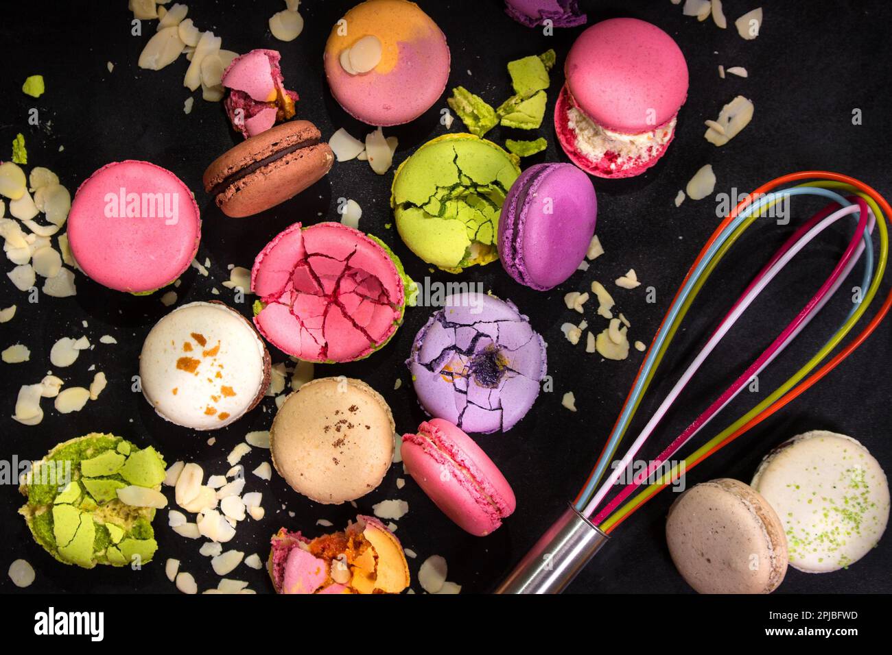 Assorted colorful french macarons and almond flakes with a whisk on a ...