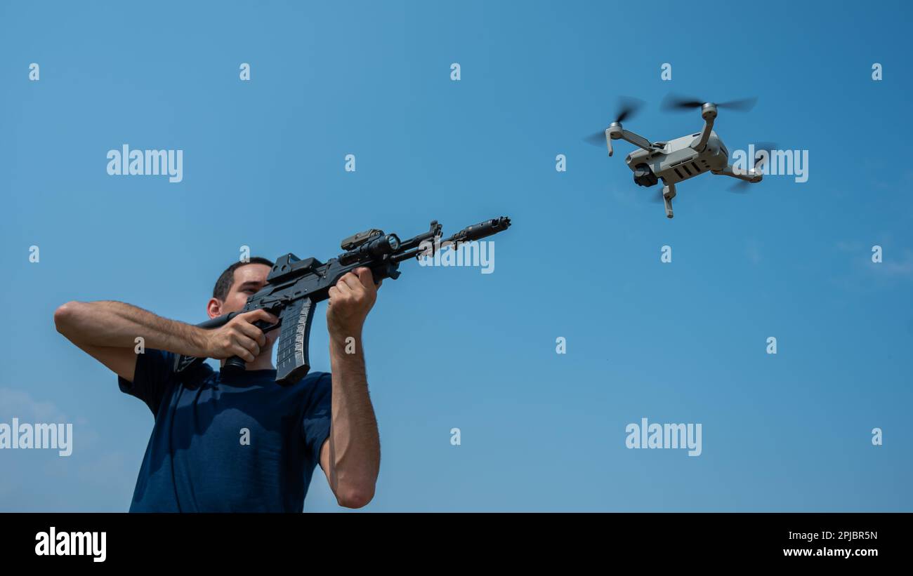 A man aims to shoot a rifle at a flying drone against a blue sky Stock ...