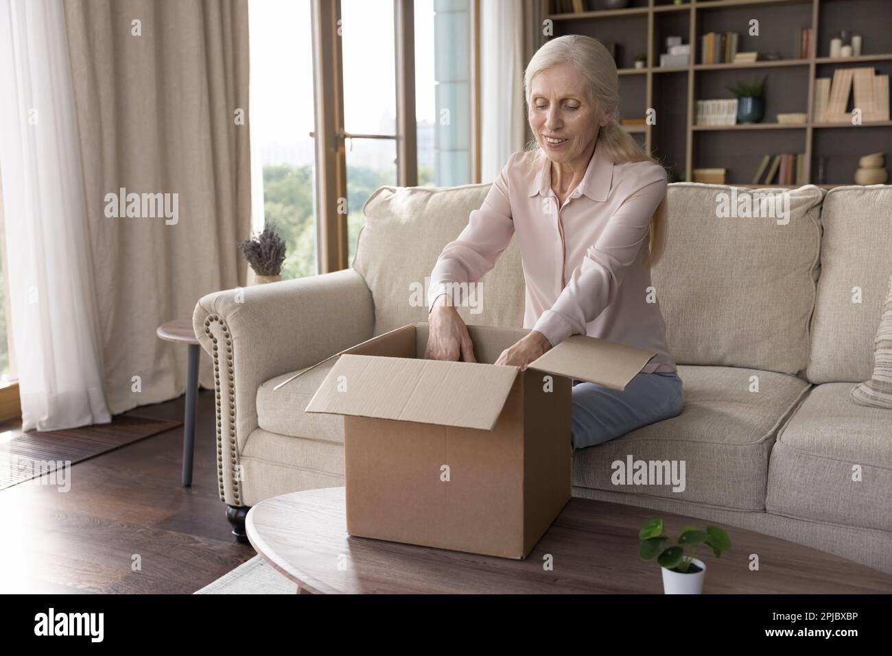 Positive older customer lady receiving parcel, opening cardboard box ...