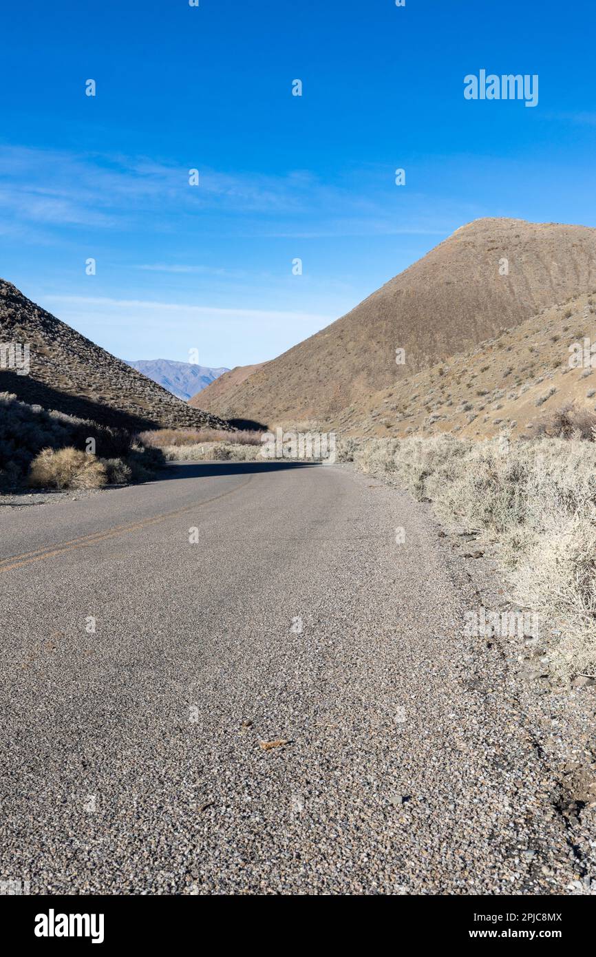 An empty paved road through scrub brush covered hills in the desert ...