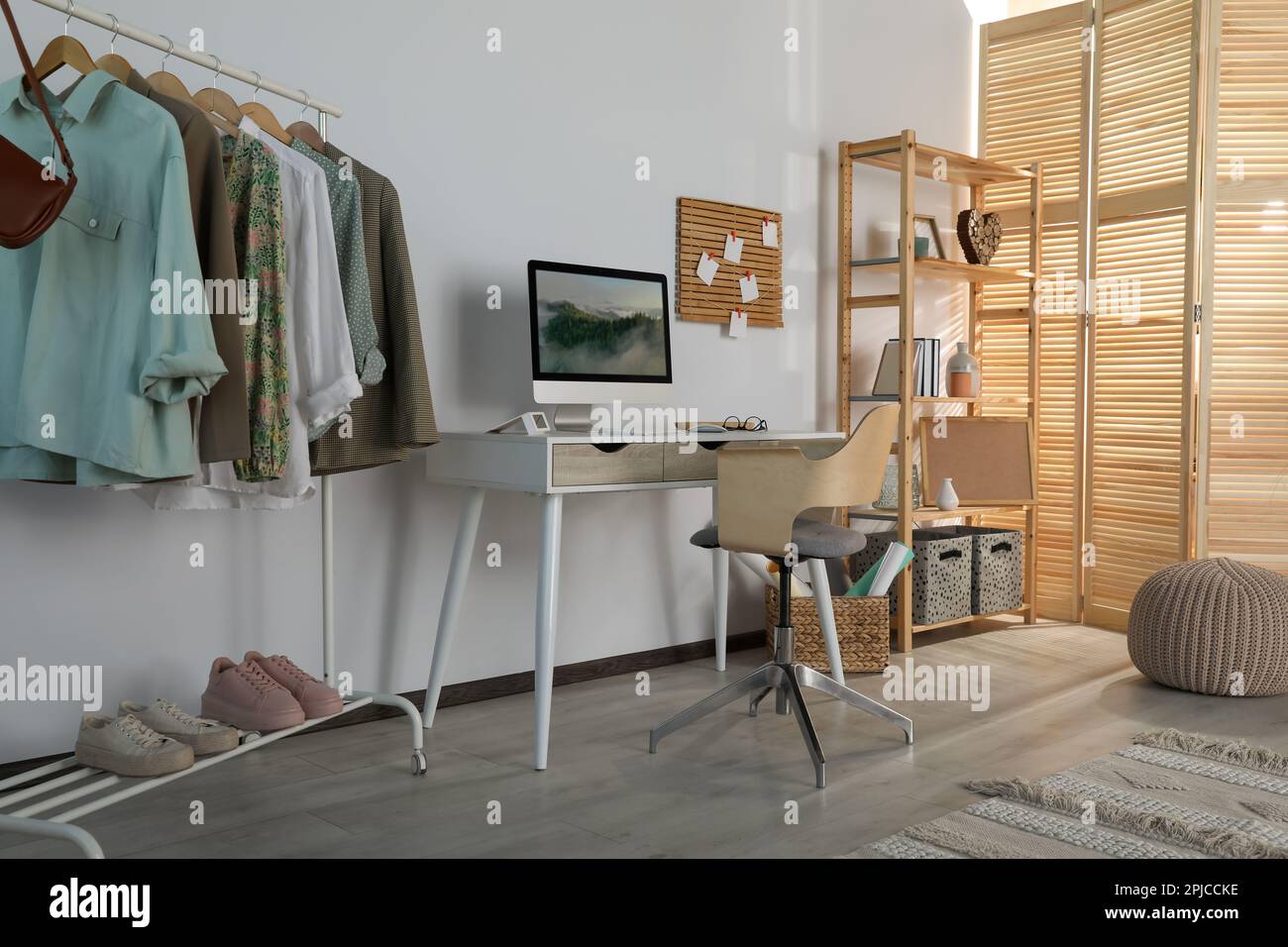 Stylish room interior with comfortable workplace and rack of clothes ...