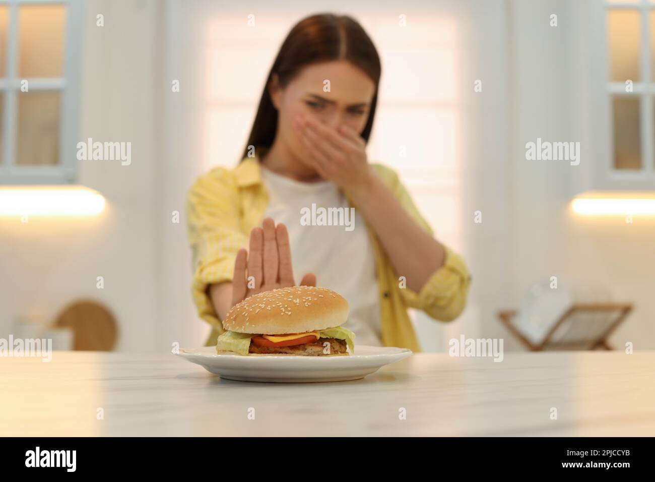 Young woman suffering from nausea at table in kitchen, focus on burger ...