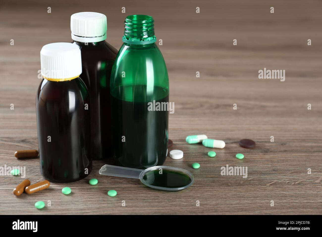 Bottles of cough syrup, dosing spoon and pills on wooden table Stock ...