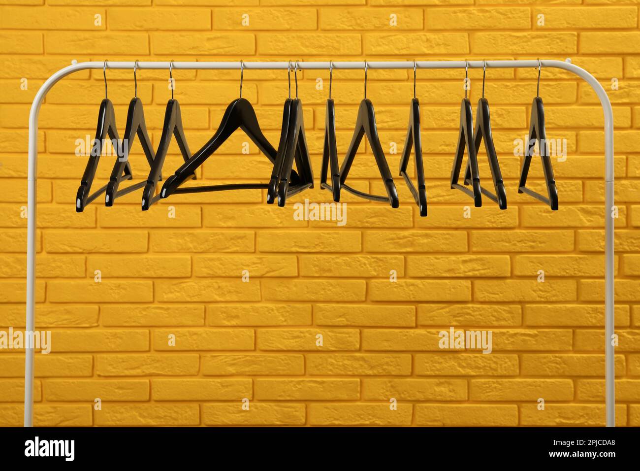 Wardrobe rack with many hangers near yellow brick wall Stock Photo - Alamy
