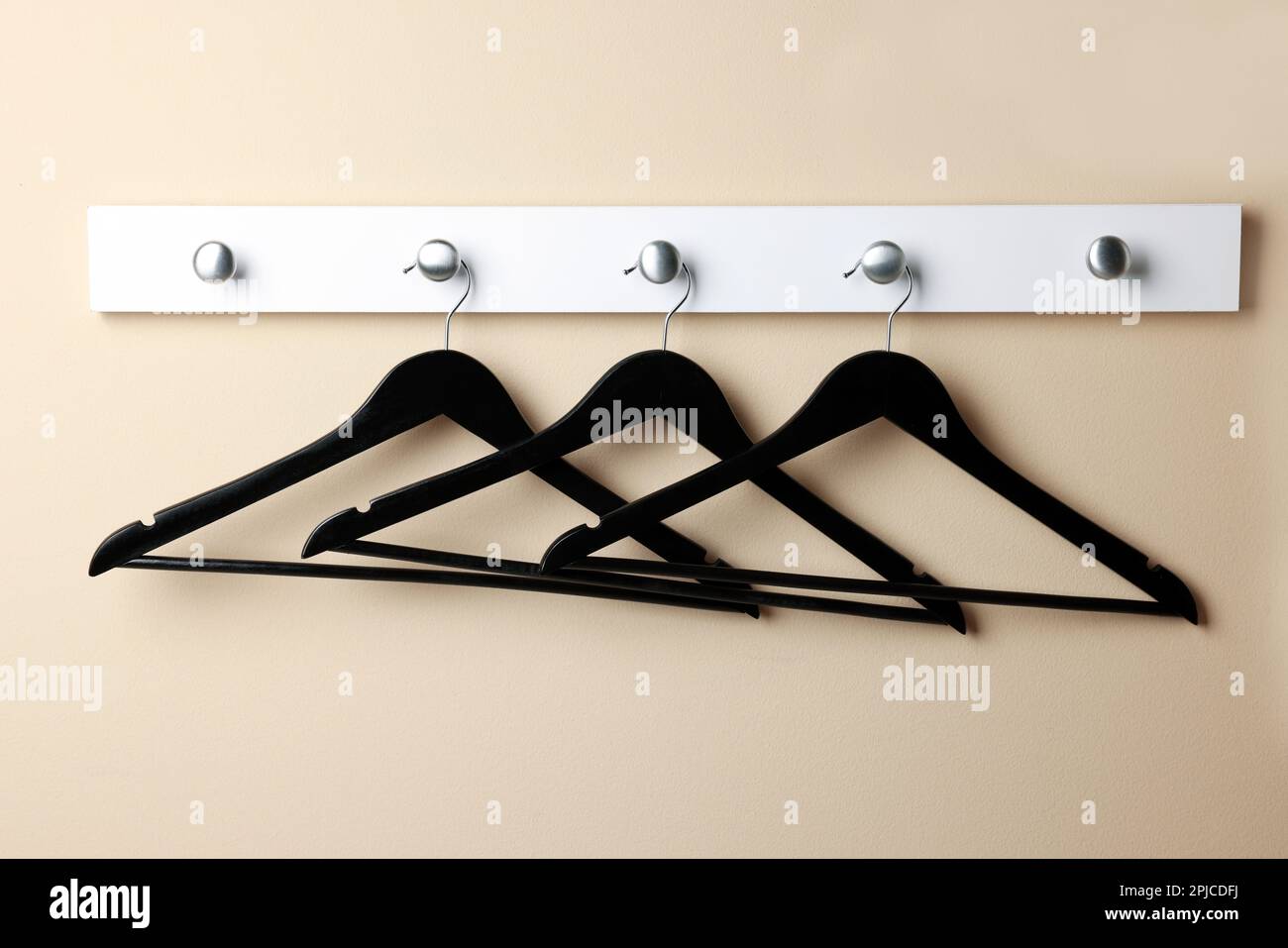 Rack with empty black clothes hangers on beige wall Stock Photo - Alamy