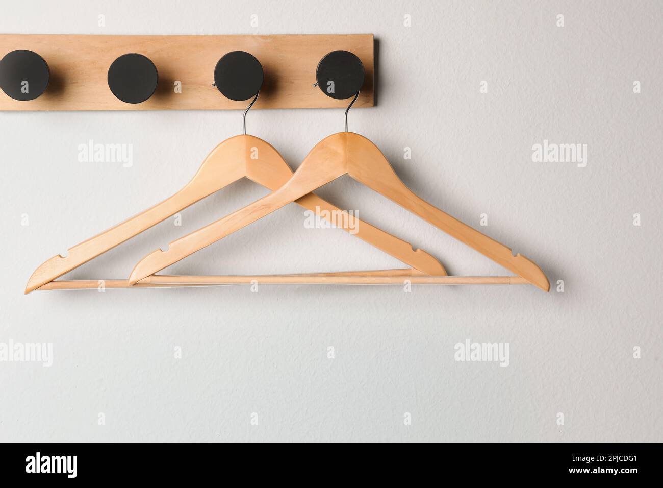 Rack with empty wooden clothes hangers on white wall Stock Photo - Alamy
