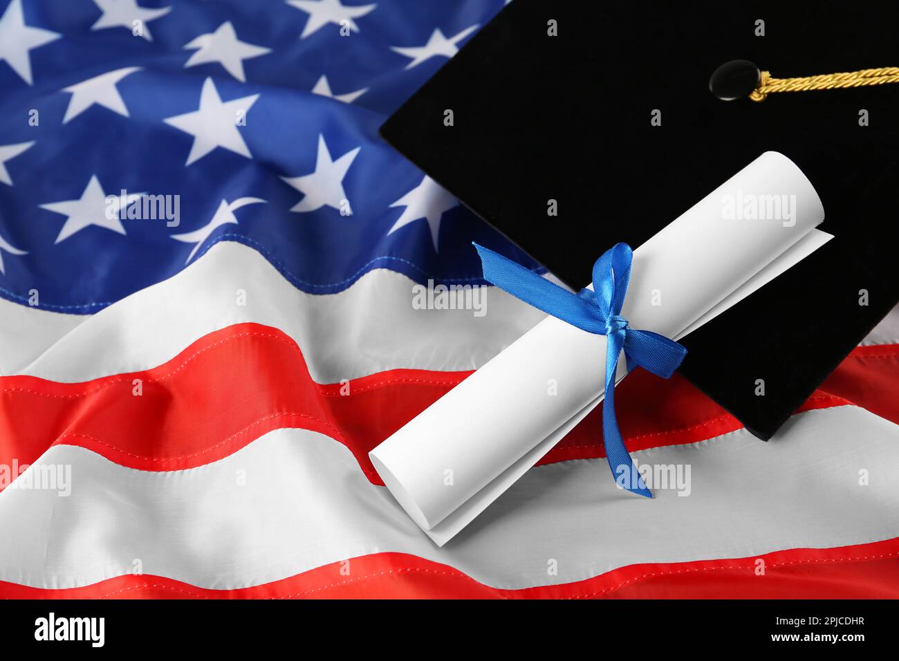 Black graduation hat and diploma on American flag, closeup. Space for ...