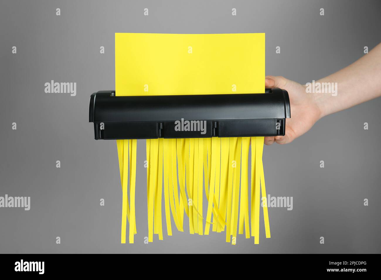 Woman destroying sheet of yellow paper with shredder on grey background ...
