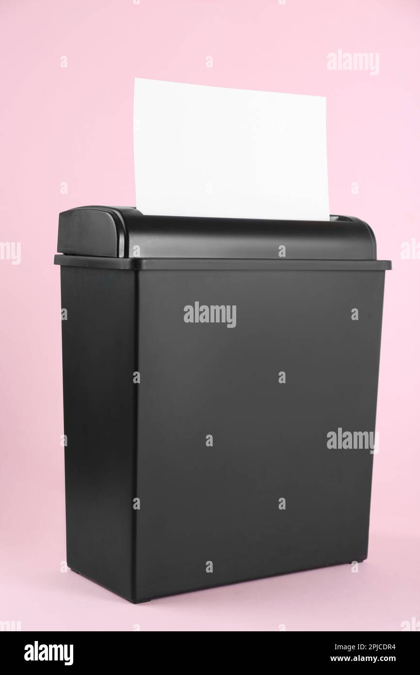 Shredder with sheet of paper on pink background Stock Photo - Alamy