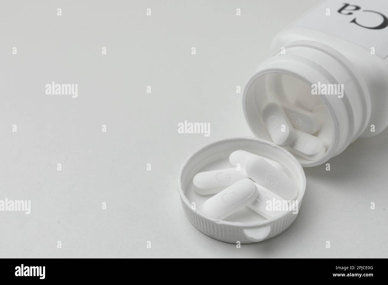 Overturned jar of calcium supplement pills on white background, closeup ...