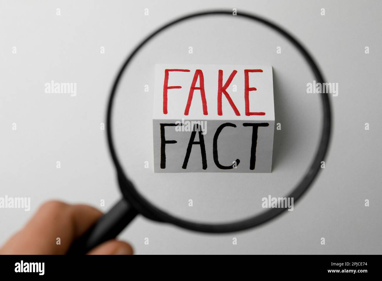 Woman holding magnifying glass over sheet of paper with words Fact and ...