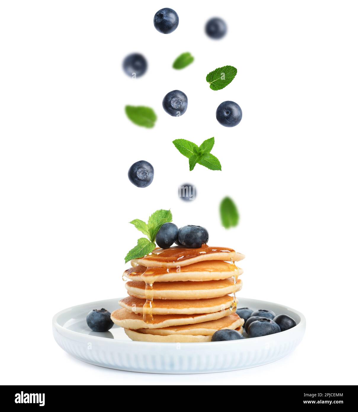Fresh blueberries and mint leaves falling onto stacked pancakes against ...