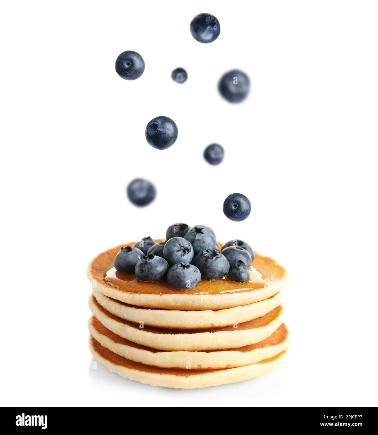 Fresh blueberries falling onto stacked pancakes against white ...