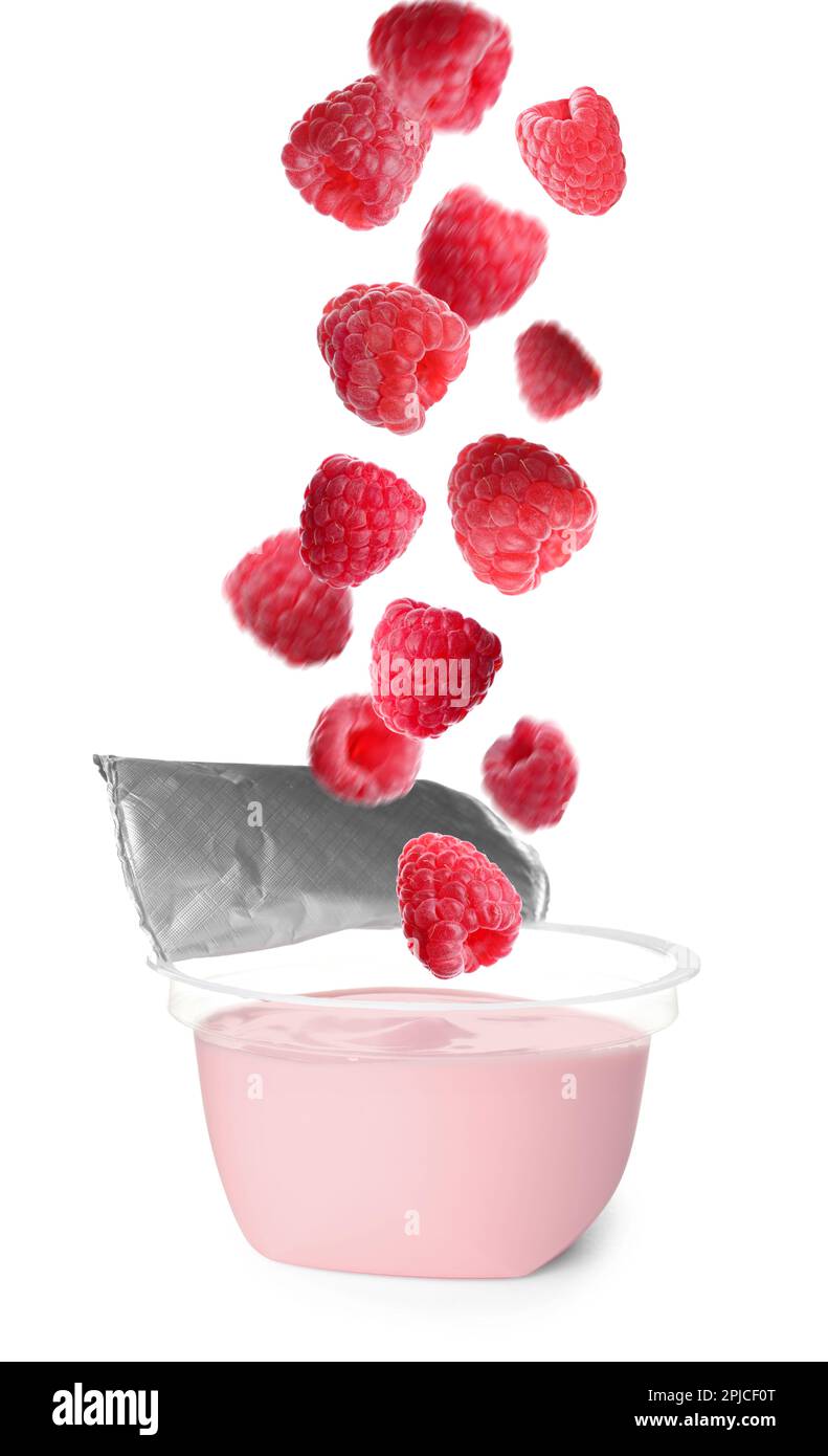 Many fresh raspberries falling into plastic cup with yogurt on white ...