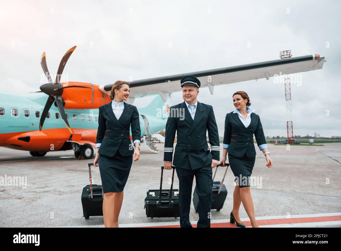 With luggage. Aircraft crew in work uniform is together outdoors near ...
