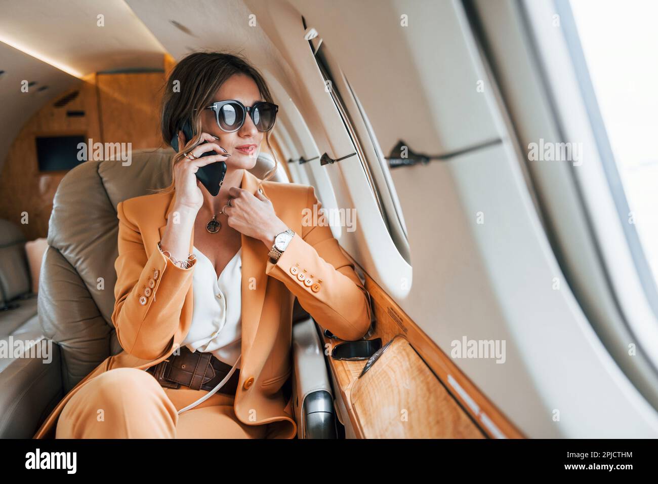 Uses phone. Young passenger woman in yellow clothes is flying in the plane Stock Photo - Alamy