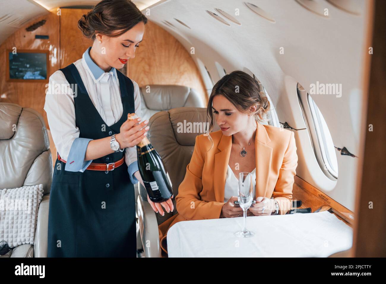 Stewardess with bottle of alcohol. Young passenger woman in yellow ...
