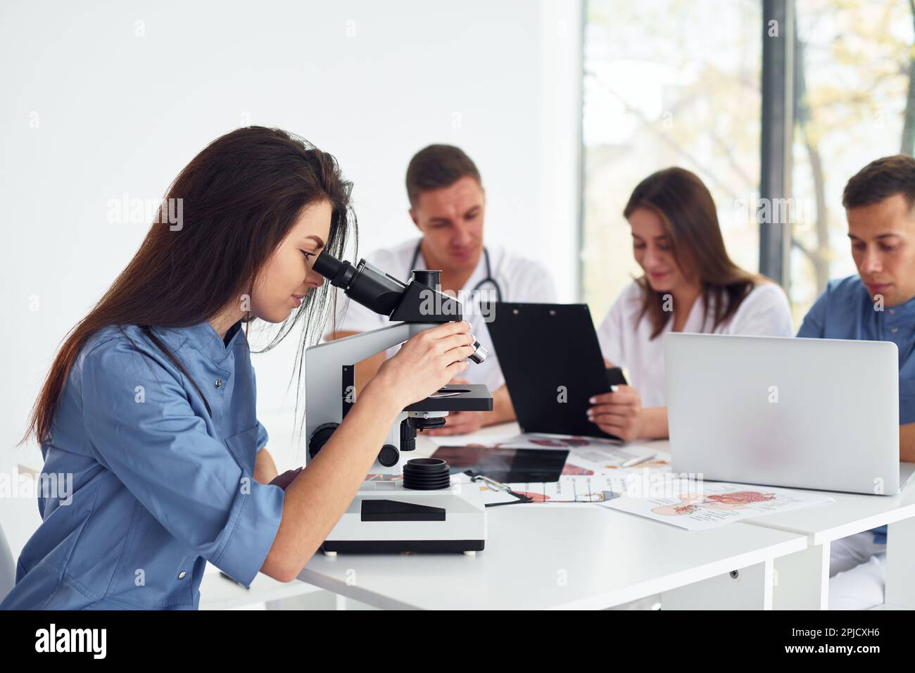 Using microscope. Group of young doctors is working together in the ...