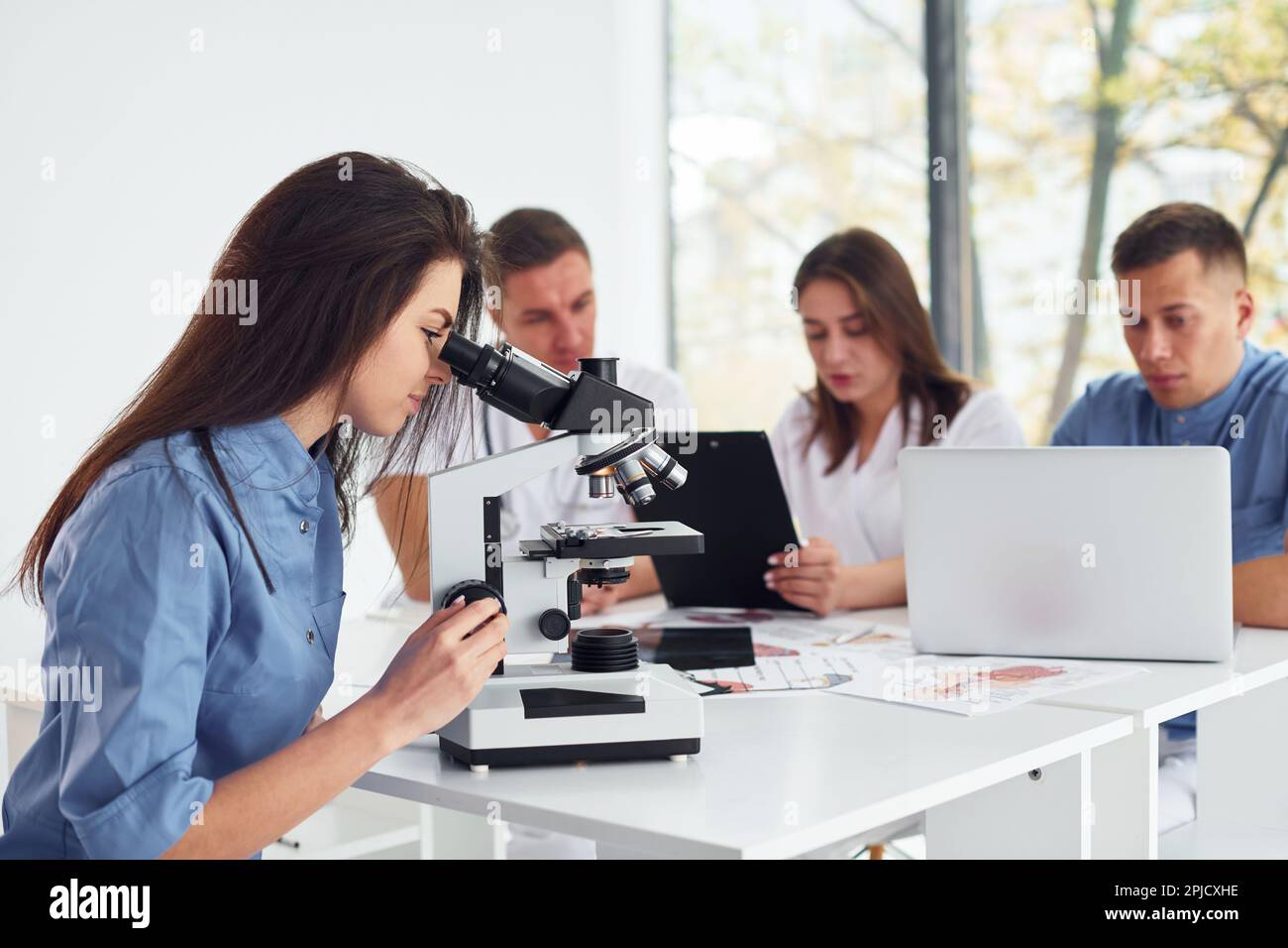 Using microscope. Group of young doctors is working together in the ...